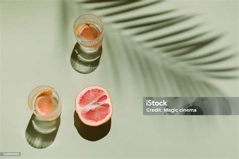 여름 플랫에는 야자수 잎 그림자 태양과 햇빛이있는 녹색 배경에 다과 음료와 자몽 조각 두 잔이 놓여 있습니다 휴가 휴일 칵테일 창조적 인 최소 개념 칵테일에 대한 스톡 사진