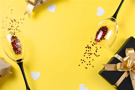 휴일 배경입니다 두 개의 깜박이는 와인 잔 노란색 배경에 분홍색 하트 색종이로 장식 된 다양한 수제 선물 상자 발렌타인 데이 컨셉 플랫 레이 상단 보기 복사 공간 개념에