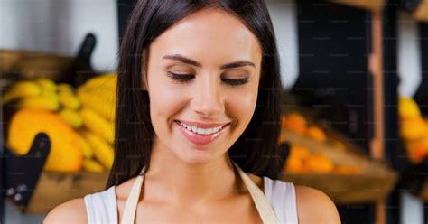 앞치마를 입은 아름다운 젊은 여성이 메모장에 메모를 하고 배경에 다양한 과일이 있는 식료품점에 서서 웃고 있다 사진 Unsplash의 기업가 정신 이미지