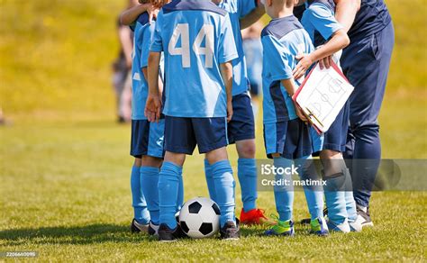 휴식 시간에 코치와 함께 원을 그리며 모여 있는 축구 선수들 코치 들고 전술 화이트 보드 하프타임에 학교 축구팀 멤버들 어린이를 위한 여름 축구 리그 청소년 스포츠 토너먼트