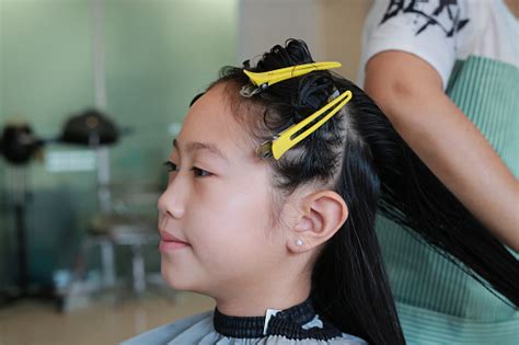 미용사가 미용실에서 귀여운 아시아 소녀 아이에게 머리를 만들고 있습니다 미용실에 있는 어린 소녀 10 11세에 대한 스톡 사진