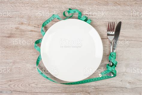 상단 보기 녹색 측정 테이프는 나무 테이블 배경에 흰색 세라믹 접시와 포크와 칼을 감싸 다이어트 체중 감소 비만 및 식품 제어 개념 0명에 대한 스톡 사진 및 기타 이미지