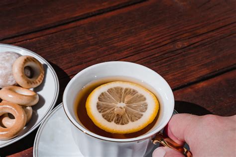 맛있는 음식과 과자와 함께 티 파티 세라믹 화이트 컵과 차 세트 레몬을 손에 들고 차 한 잔을 들고 있습니다 갈색에 대한 스톡