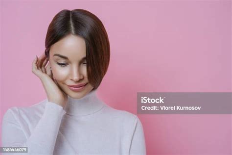 수줍은 젊은 여성의 사진은 아래를 내려다 보고 캐주얼 한 옷을 입고 꿈꾸는 표정을 가지고 장밋빛 배경 승진을위한 빈 공간에 대해 쾌적하고 고립 된 것에 대해 생각합니다 25