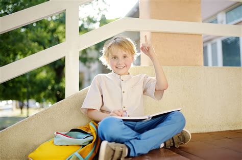초등학교 건물 계단에서 휴식 시간에 숙제를 하는 어린 학생 아이디어를 가지고 집게 손가락을 보여주는 귀여운 소년 통찰력 개념입니다 학교 개념으로 돌아갑니다 작은 아이들을위한