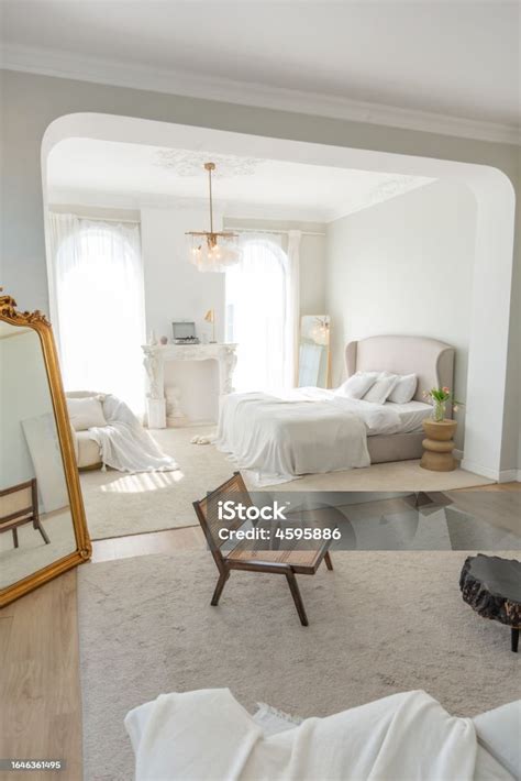 햇살이 내리쬐는 거대한 파노라마 창문이 있는 아늑하고 밝은 아파트 흰색과 베이지색 톤의 침실에는 벽난로와 부드러운 안락의자가 있습니다 통나무 커피 테이블과 대형 흰색 소파가