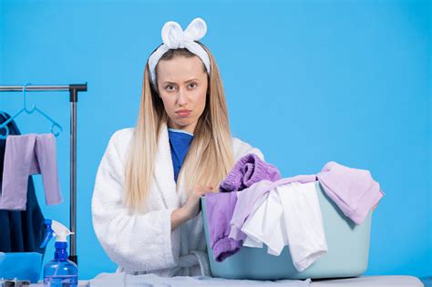성인 재미있는 여자는 다리미판에 신경질적으로 기대는 바보 같은 얼굴을 만듭니다 소녀는 혼자 집안일을하고 옷을 접는 것에 지쳤다