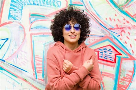 젊고 예쁜 아프리카 여자 쾌활하게 웃고 축하 꽉 주먹으로 팔을 넘어 낙서 벽에 행복하고 긍정적 인 느낌 프리미엄 사진