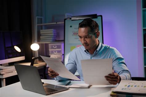 열심히 일하는 아시아 사업가는 자신의 프로젝트에 집중하고 손에 서류를 들고 사무실에서 혼자 밤에 초과 근무를합니다 Business Model Strategy에 대한 스톡