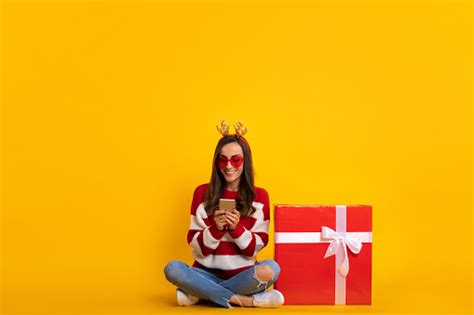 그녀가 큰 빨간 선물 상자와 스마트 폰을 사용하는 동안 행복 젊은 미소 아름답고 매력적인 여자의 전체 길이 사진 크리스마스 순록 뿔 12월에 대한 스톡 사진 및 기타 이미지