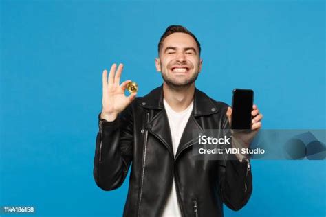 검은 자 켓 흰색 T 셔츠에 잘생긴 세련 된 젊은 면은 남자는 손 핸드폰 비트 코인 파란색 벽 배경 스튜디오 초상화에 고립 된 통화를 개최 합니다 사람들 라이프 스타일
