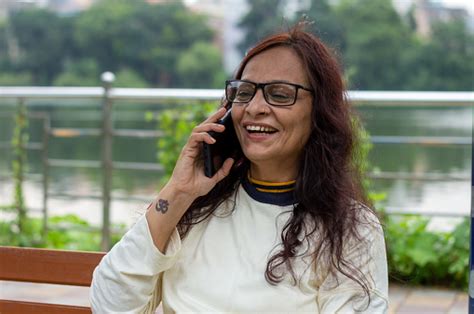 긴 갈색 머리를 가진 웃는 여자 야외에서 편안한 휴대 전화로 말하기 근접 촬영 그녀는 흰색 티셔츠와 사양을 입고 있습니다 정면도 머리와 어깨 샷 말하기에 대한 스톡 사진 및