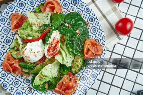 흰색 배경의 아름다운 파란색 세라믹 플레이트에서 연어 시금치 데친 달걀 및 리코타를 곁들인 식욕을 돋우는 샐러드를 가까이에서 볼