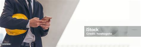 스마트 폰을 들고 노란색 하드 모자를 들고있는 배너 건설 엔지니어 파노라마 안전 헬멧 전화 건설 현장을 사용하여 노란색 하드 햇을 들고 복사 공간이있는 배너 Hardhat