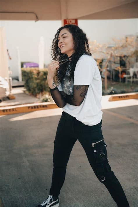 거리 거리 스타일 거리 패션 걱정 없는 검은 색 바지 곱슬머리 도시의 라이프스타일 문신 미소 짓는 서 있는 스니커즈 스타일리시한 시원한 야외 패션