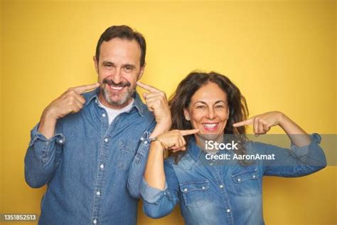 아름다운 중년 부부는 함께 고립 된 노란색 배경 위에 서서 웃으며 손가락 이빨과 입을 가리키며 쾌활한 미소를 지었습니다 치과 건강 개념 커플에 대한 스톡 사진 및 기타