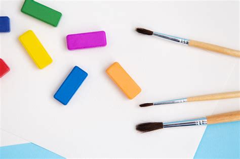 여러 가지 색상의 페인트 다양한 크기의 수채화 브러시는 파란색 배경에 수채화 종이와 함께 놓여 있습니다 레슨 그리기 위에서 볼