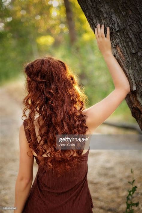 Back View Of Woman With Long Curly Red Hair In Forest Touching Tree