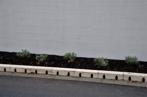 아스팔트 도로 가장자리에 숨겨진 배수 구멍이 뚫린 콘크리트 회색 연석에 숨겨진 배수 시스템 도로의 전체 길이를 따라 물이 구멍을 통해 하수구로 배수되고 잔디 묶기 투과성의에