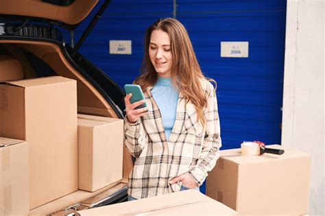 자동차 트렁크에 휴대폰과 골판지 상자를 들고 창고로 들어가는 행복한 아가씨 상자에 대한 스톡 사진 및 기타 이미지 상자 신체 활동 차 Istock