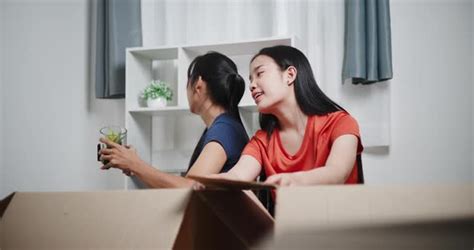 Two Happy Asian Women Are Helping To Decorate A Shelf In Their Living