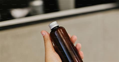 플라스틱이 없는 천연 유기농 필수품이 있는 세련된 검은색 선반을 배경으로 현대적인 욕실의 유리병에 천연 강장제 또는 샴푸를 들고