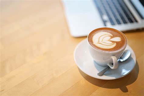 나무 테이블 위에 놓인 커피 라떼 한 잔의 클로즈업 이미지 배경에 컴퓨터 노트북이 있는 공간 책상에 대한 스톡 사진 및 기타