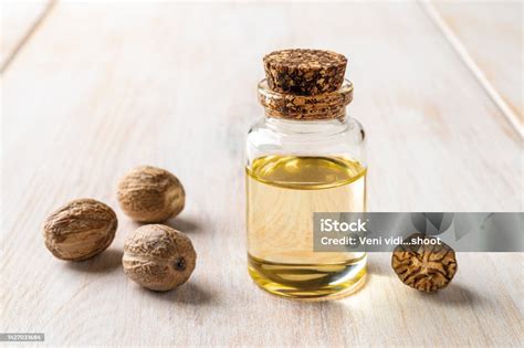 육두구 에센셜 오일 클로즈업의 유리 항아리 육두구 향기로운 기름과 씨앗은 하얀 나무 배경 위에 작은 병에 담겨 있습니다 Myristica Fragrans 나무 과일