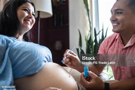 임신 한 아내의 배를 성별로 그리는 남편이 집의 거실에서 드러납니다 25 29세에 대한 스톡 사진 및 기타 이미지 25 29세 30 34세 가정 생활 Istock