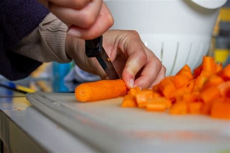 날카로운 칼로 부엌의 커팅 보드에 당근을 작은 조각으로 자르는 사람의 초상화 오렌지 야채는 저녁 식사를위한 멋진 식사에 사용할