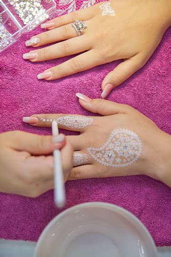 주인은 흰색 젤과 그의 손에 부타 깃털의 형태로 그립니다 거리 예술가는 도시 휴가에 자신의 손에 헤나 패턴을 그립니다 손톱에 분홍색 바니시 헤나를 그의 손에 그립니다 갈색에