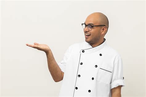 미소 짓는 젊은 잘 생긴 아시아 남자 요리사는 안경을 착용하고 서있는 채로 손바닥을 들고 고립 된 메뉴를 들고 게시합니다 요리 남자 직업 요리사 부엌 레스토랑과 호텔에있는