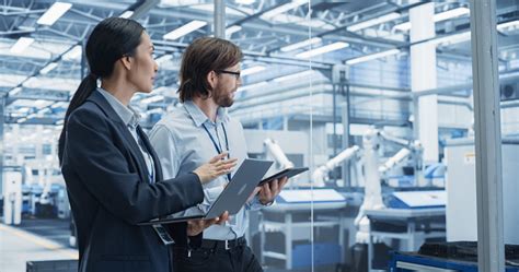 쾌활한 엔지니어와 행복한 아시아 과학자가 노트북과 태블릿 컴퓨터를 사용하여 공장 시설에서 다양한 산업을 위한 최신 전자 부품을