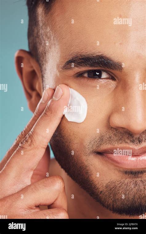 Closeup Of One Young Indian Man Applying Moisturiser Lotion To His Face While Grooming Against A