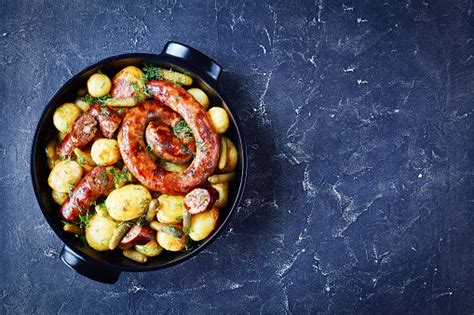 구운 새로운 감자와 이탈리아 돼지 고기 소시지를 거킨과 검은 접시에 볶고 어두운 콘크리트 배경에 딜을 뿌렸습니다 소시지에 대한 스톡 사진 및 기타 이미지 Istock