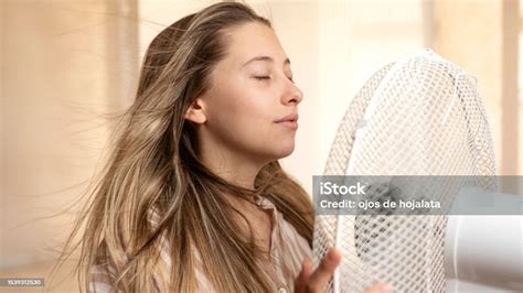 극한의 온도 여름 더위 집에서 선풍기로 몸을 식히고 극심한 여름 폭염 동안 선풍기의 시원한 공기로 폭염 동안 고온과 싸우는 젊은 여성 열 개념에 대한 스톡 사진 및 기타