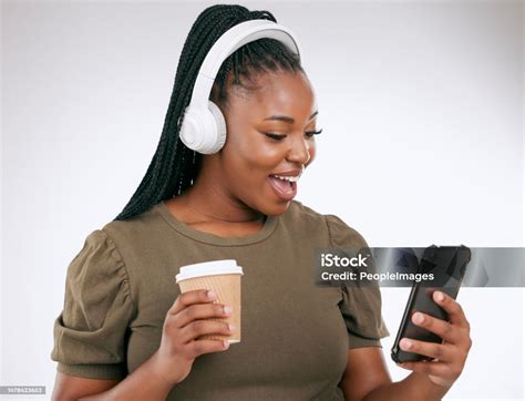 음악 커피 그리고 라디오를 듣고 있는 회색 배경의 스튜디오에서 흑인 여성과 놀람 전화 소셜 미디어 또는 헤드폰 및 음료와 함께 오디오 재생 목록을 스트리밍하는 젊은 여성