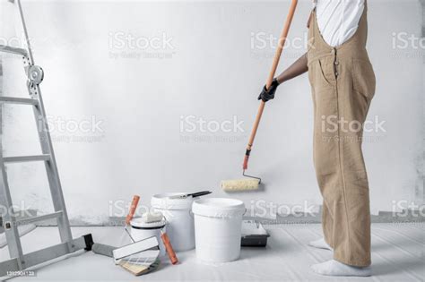 한 남자가 롤러로 하얀 벽을 그립니다 내부의 수리 빈 방에 벽을 그리는 젊은 남성 데코레이터 개념 빌더 또는 빈 방에 페인트 롤러와 헬멧에 화가 40 44세에 대한 스톡