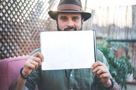 매력적인 Hipster 블로거 카페의 테라스에서 시간을 보내는 동안 손에 오픈 빈 시트와 메모장을 들고 복사 붙여넣기 텍스트