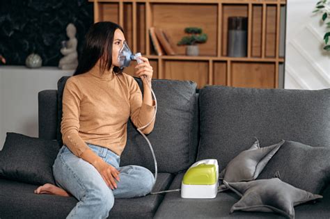 흡입기를 가진 아픈 화가 백인 갈색 머리 여자 건강에 해로운 여성은 집에서 흡입을하고 치료를 위해 분무기와 흡입기를 사용하고 집에서 소파에 앉아 치료가 필요합니다