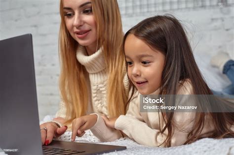 아름 다운 젊은 어머니와 흰색 스웨터와 청바지에 그녀의 귀여운 딸 집에서 침대에 누워 웃 고 노트북에 보고 가정의 방에 대한 스톡 사진 및 기타 이미지 Istock
