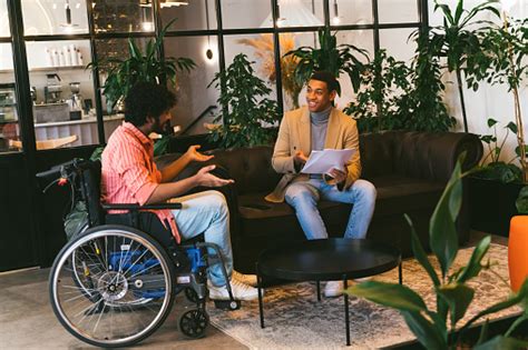 사무실 리셉션 룸에서 혼합 인종 임원 동료 회의 및 현대 사무실 공동 작업 장소의 휴식 공간에서 아이디어를 교환 휠체어를 탄 장애인 인도 사업가 20 24세에 대한 스톡