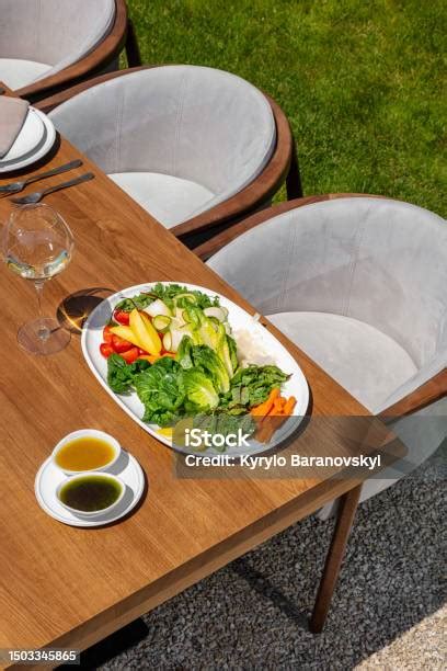 다양한 종류의 채소와 파마산 치즈를 곁들인 야채 접시 근처에는 소스가 담긴 그릇 두 개가 있습니다 접시는 나무 테이블 가장자리에 있습니다 근처에는 의자 잔디밭 자갈이