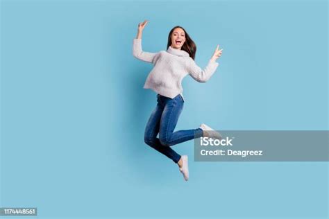 콘텐츠 솔직한 소녀 점프의 전체 길이 사진은 V사인이 미친 착용 데님 청바지 화이트 풀오버 흰색 운동화 를 파란색 배경 위에 고립 된 느낌으로 만드는 자유 시간을 가지고