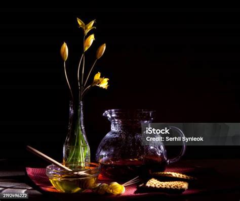 양조용 유리 찻주전자 노란색 수선화 꽃 쿠키가 담긴 고리 버들 바구니 컵 어두운 배경에 꿀이 담긴 유리 투명 그릇으로 구성된 정물 구도에 대한 스톡 사진 및 기타 이미지
