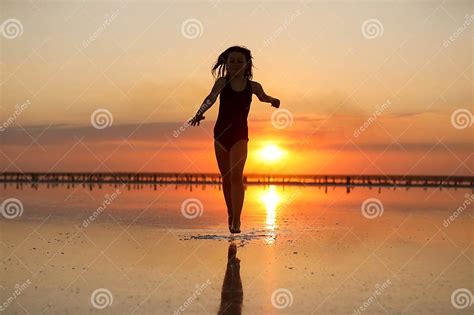 силуэт активной маленькой девочки в купальнике веселится и играет на пляже на закате в летнем