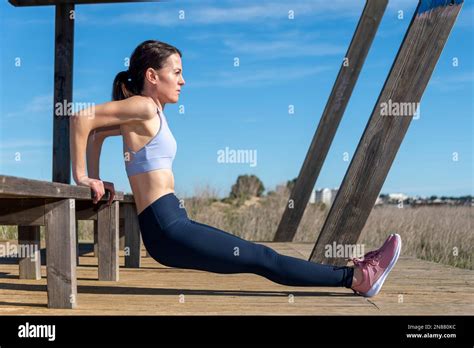 Sporty Woman Doing Reverse Push Ups Outside On A Wooden Bench Stock