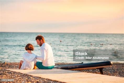 행복한 가족은 조약돌 해변에 앉아서 수영 후 휴식을 취합니다 뒤로보기 일몰 빛 공간을 복사합니다 바다에서의 여름 방학 2명에 대한 스톡 사진 및 기타 이미지 Istock