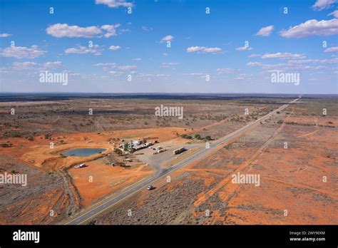 Aerial View Of A Highway Traveling Through Arid Landscape With A Small Roadside Settlement And