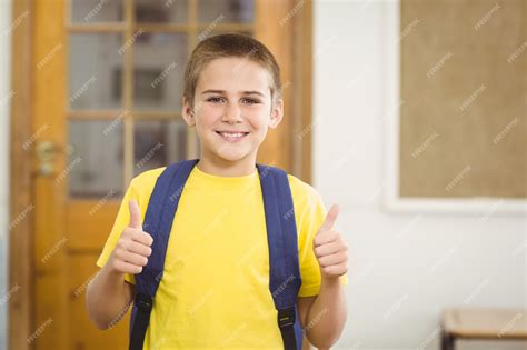 Premium Photo Smiling Pupil With Schoolbag Doing Thumbs Up In A Classroom